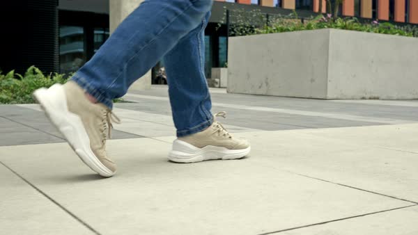 Women's legs in sneakers and jeans walk along the pavement, paved with ...