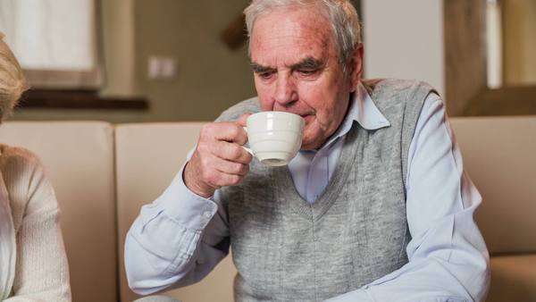 Grandpa on sofa drinking tea from cup. Middle shot of grandfather sit ...