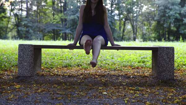 Attractive woman dangling legs on bench. Female person in blue dress ...