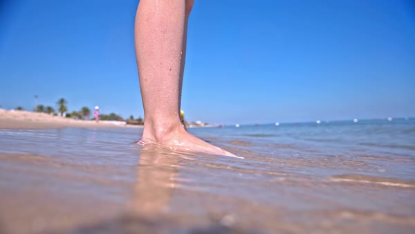 Person legs stand next to sea with water splashing. Low angle camera ...