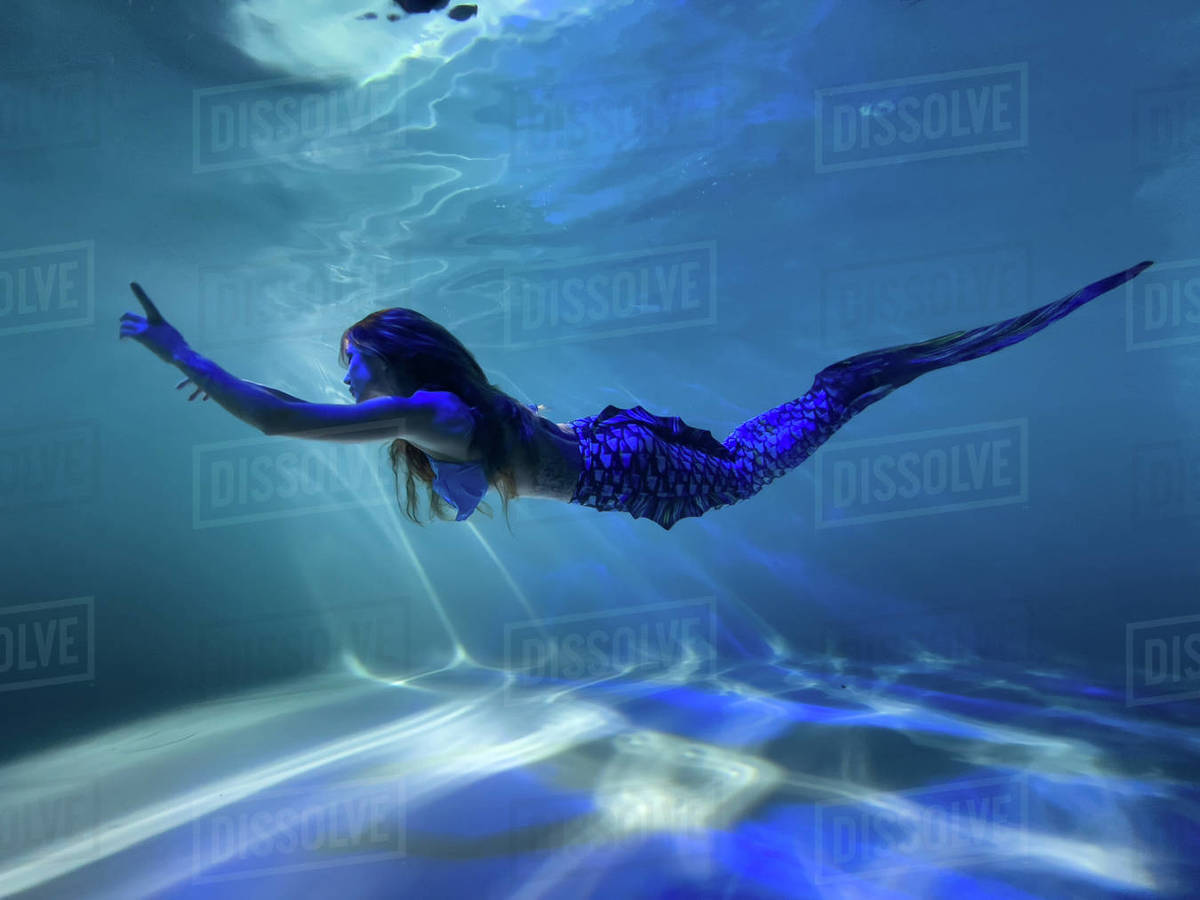 Beautiful young woman with mermaid tail swims and dives under sunlit ...