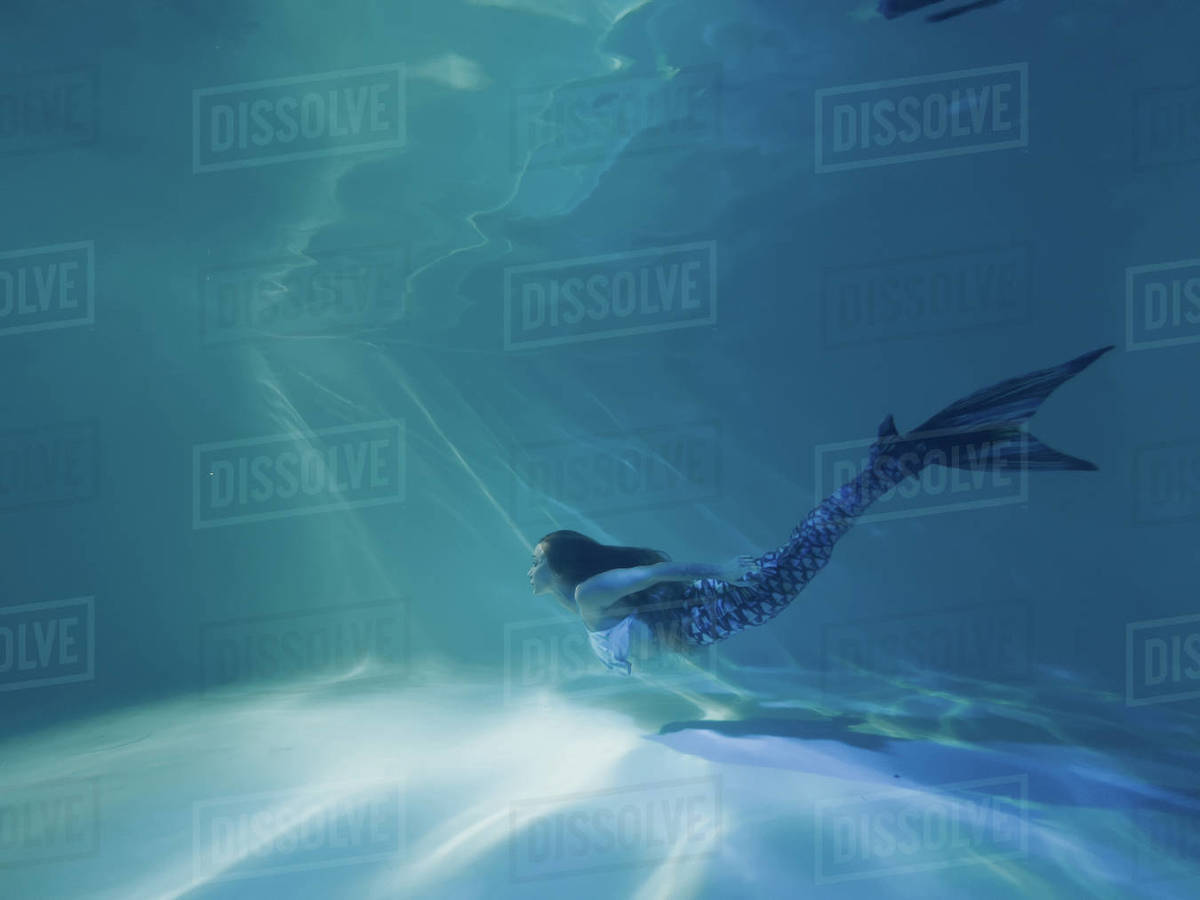 Beautiful young woman with mermaid tail swims and dives under sunlit ...