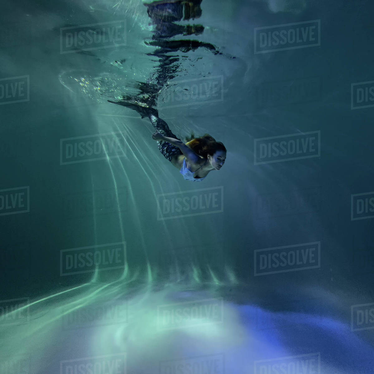 Beautiful young woman with mermaid tail swims and dives under sunlit ...