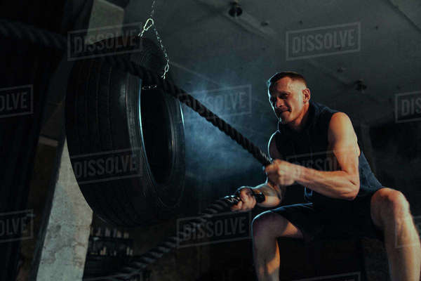 Strong muscular man exercising in dark gym with fighting ropes. Ropes ...