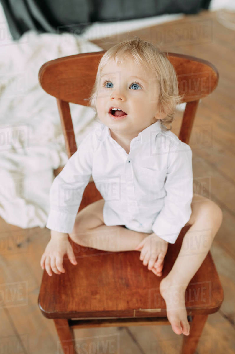 Happy toddler sits on chair and looks up. - Stock Photo - Dissolve