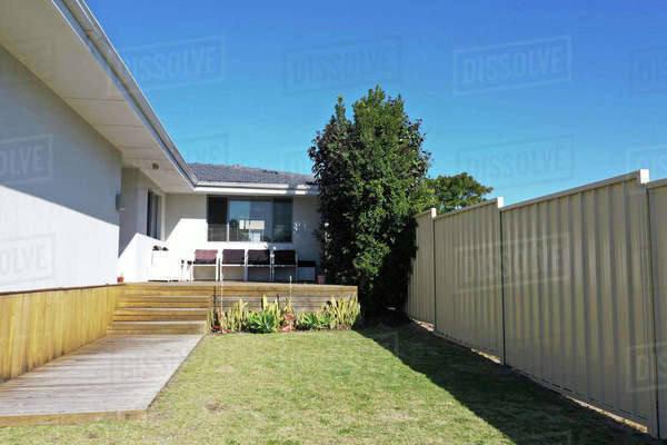 Empty home front yard with green grass and a deck under clear blue sky ...