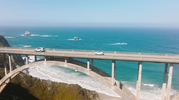 Cars driving slow by scenic arch architecture bridge with blue ocean ...