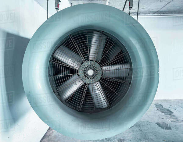 A large, gray, industrial fan is suspended from the ceiling of a ...