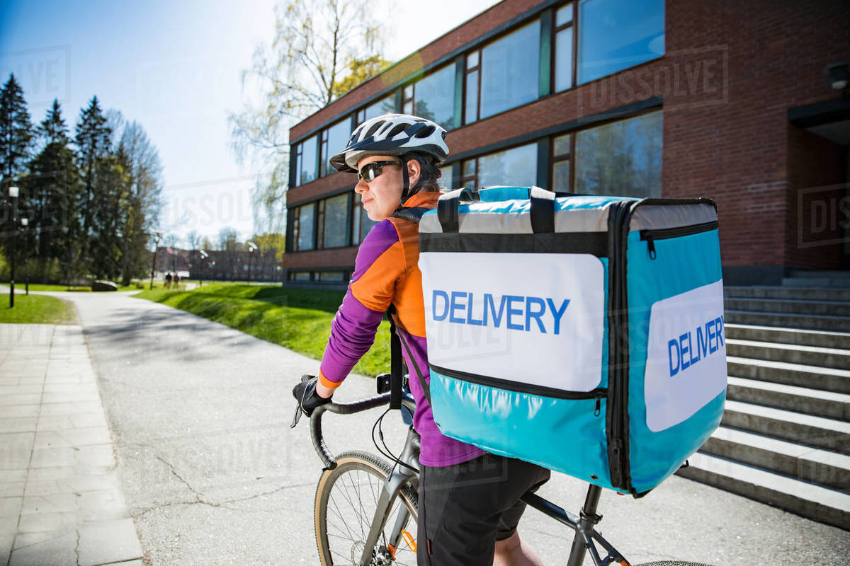 Woman in helmet with big food delivery backpack riding bike on the ...