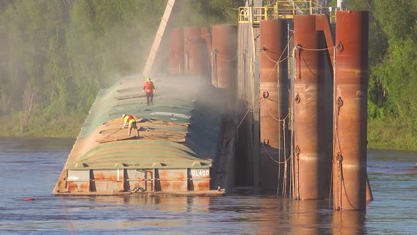 Workers load a grain barge along the Mississippi River near a large ...