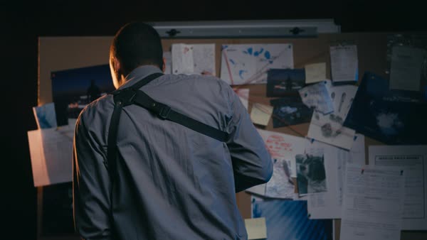 Back view of police detective looking at photos and documents on ...