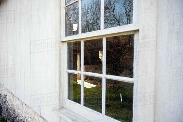 Antique window reflects nature in a whitewashed wooden colonial ...
