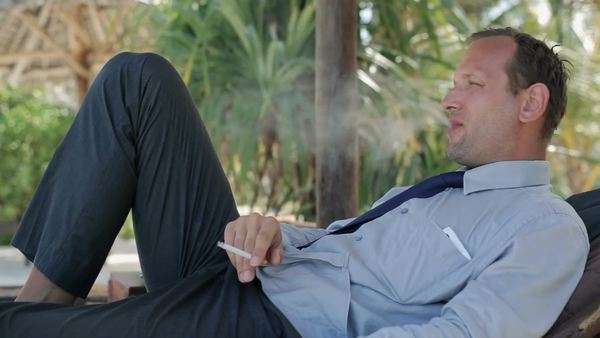 Businessman smoking cigarette and relaxing on sunbed in luxury resort ...
