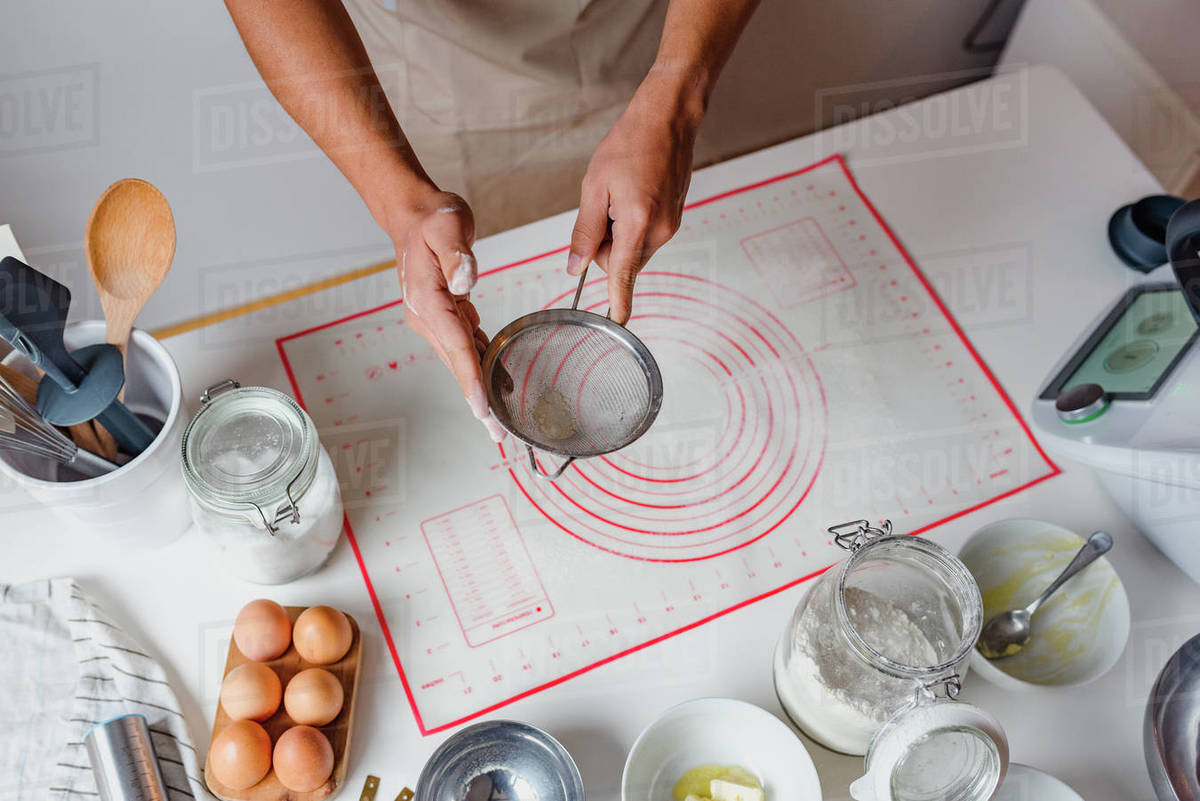 Closeup shot of hands of a man sifting flour by a sieve in a glass bowl ...
