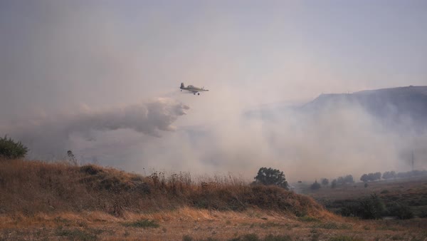 Small firefighting airplane drops fire retardant on burning grass field ...