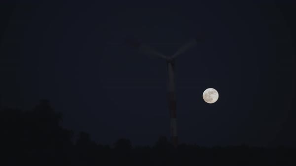 Time lapse of wind turbine rotating against the full moon background at ...
