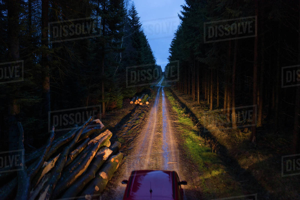 Aerial shot at night just above a red car on a dirt road in the middle ...