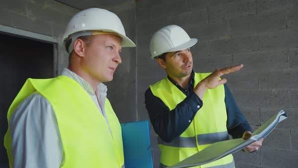 Men wearing helmets and safety vests talking in empty room with brick ...