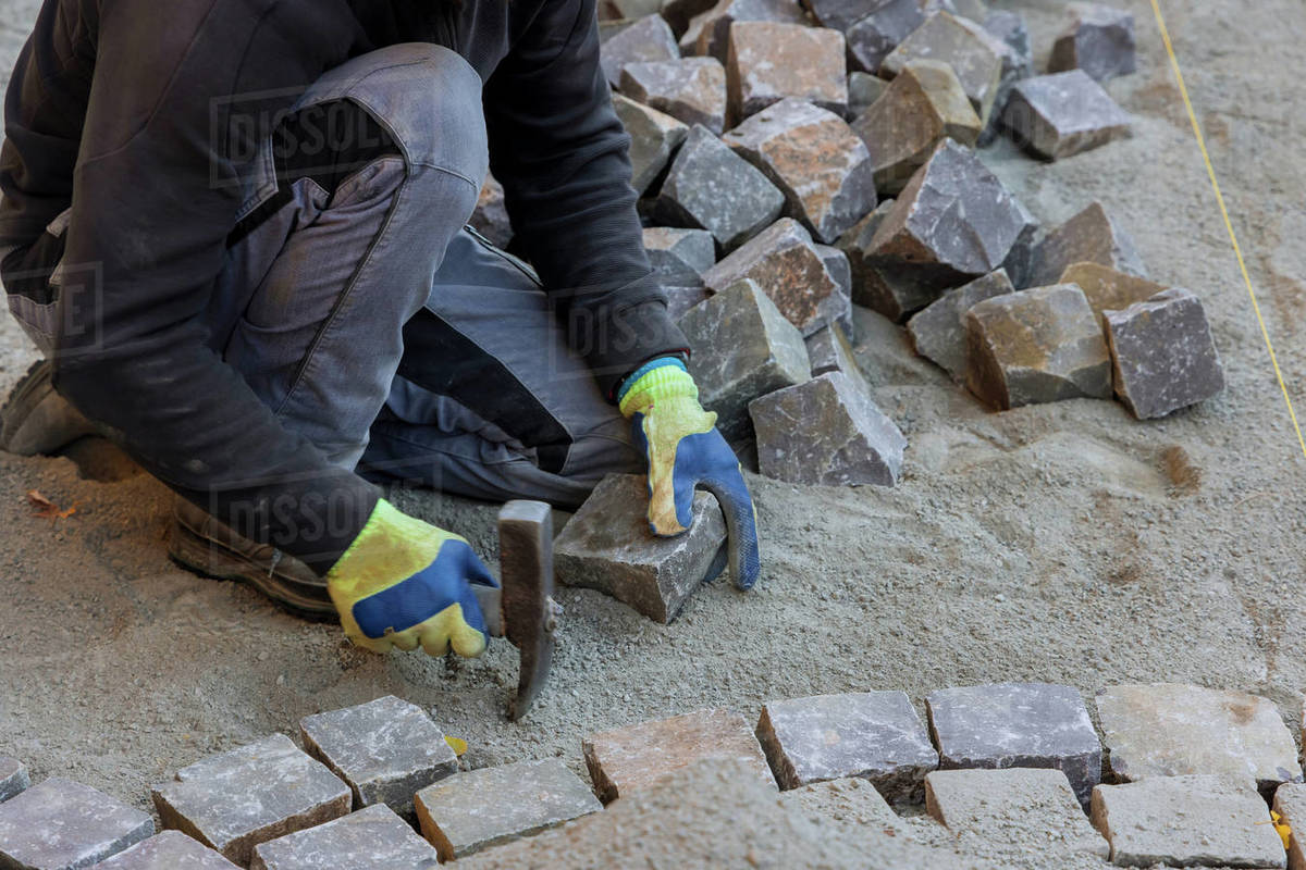 Road master of gloves lays paving stones in layers stone road by ...