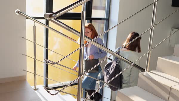Two women walk up the stairs in the office. business people or students ...