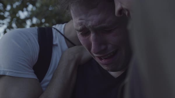 Hand-held shot of a young man crying and being comforted by his friends ...