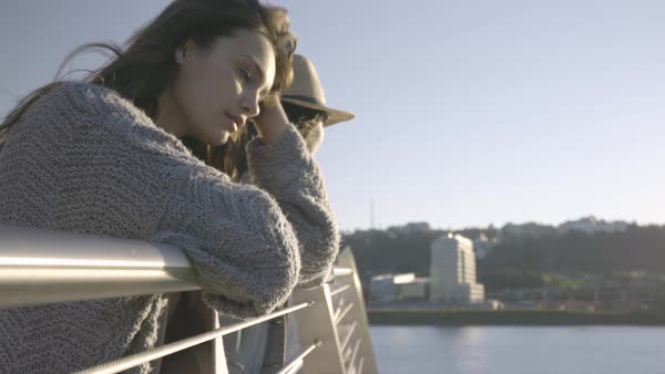 Women lean against railing and enjoy river/city views, train passes by ...