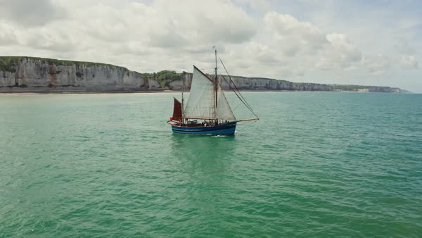 The sailing ship moves from the land, with picturesque sheer cliffs ...
