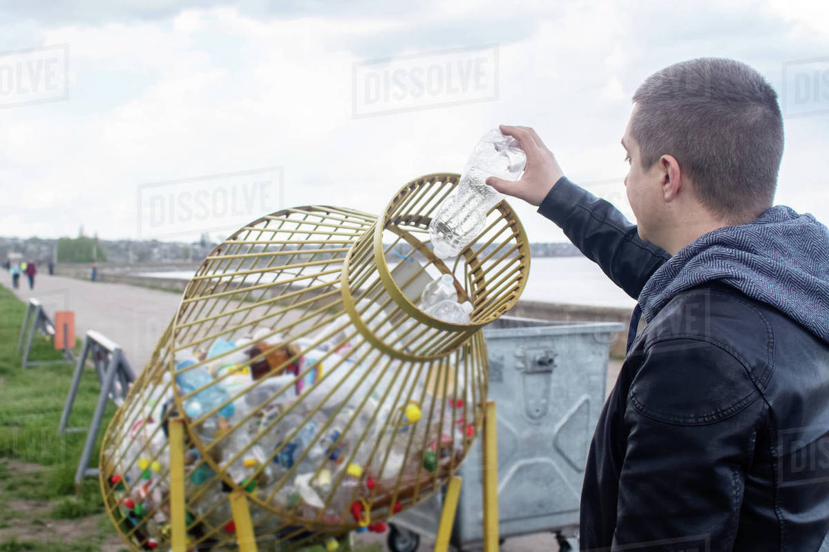 A man tosses a plastic bottle into a plastic container for collection ...