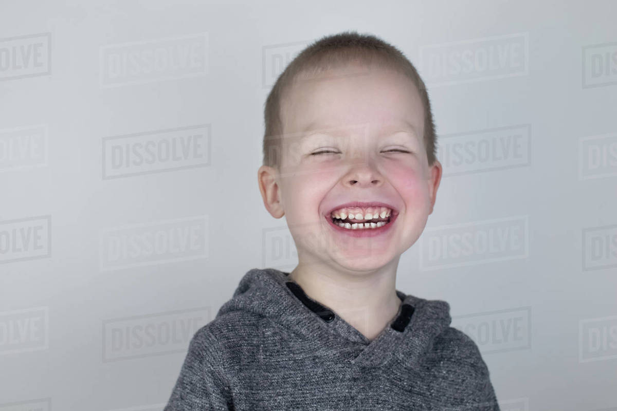 Close-up of a blond boy who smiles into the frame. White milk teeth ...