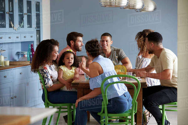 Friends with a child sit talking around a dining room table - Royalty ...