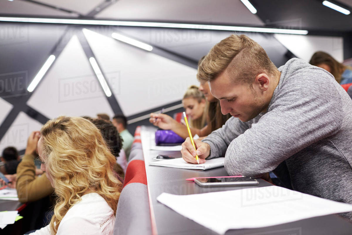 Male student taking notes in a university lecture theatre - Royalty ...