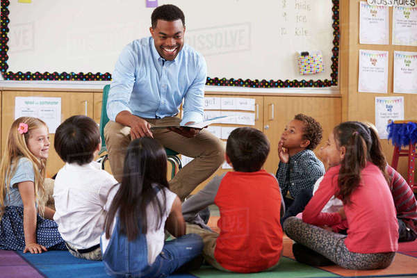 Elementary school kids sitting around teacher in a classroom - Royalty ...