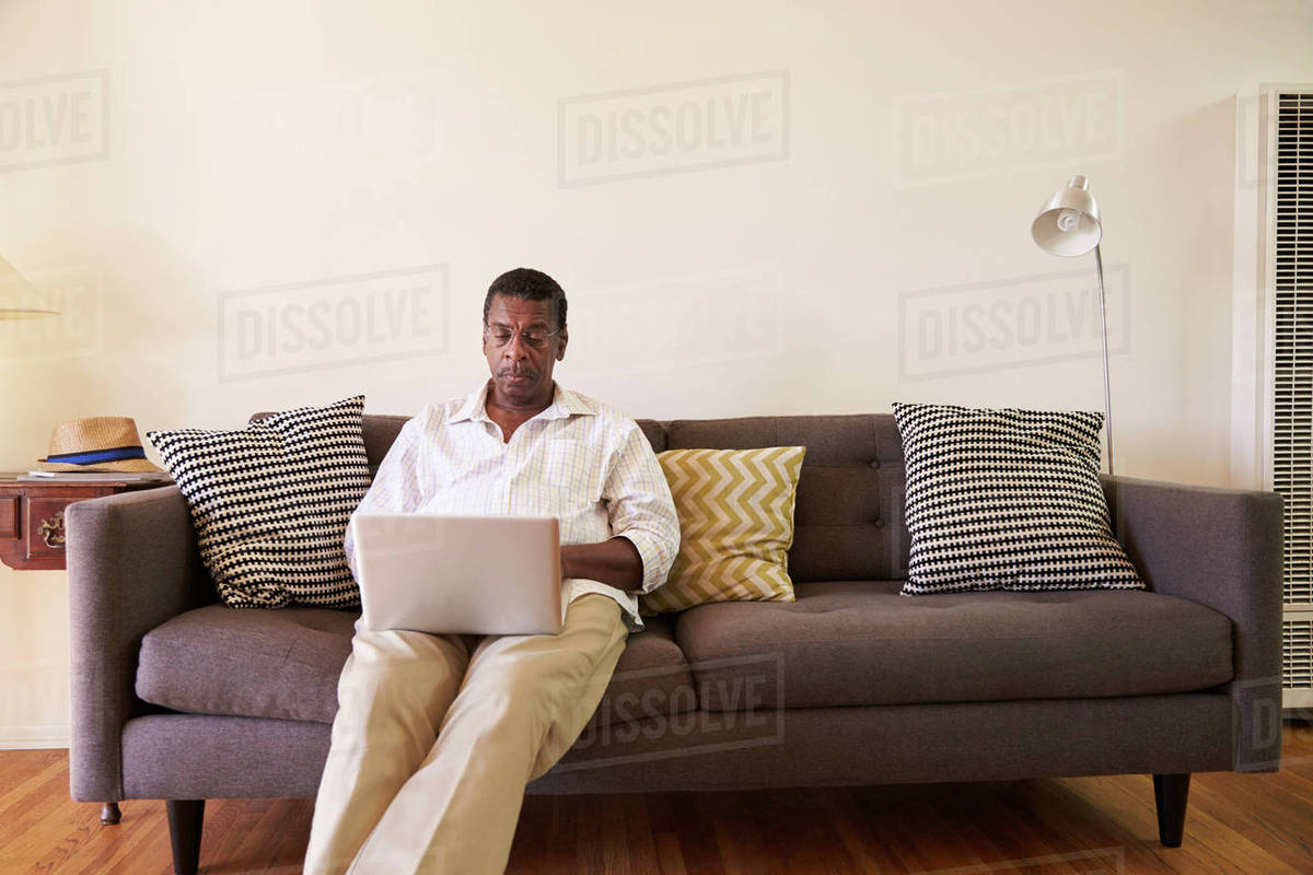 Senior man sitting on sofa at home using laptop - Royalty-free Stock ...