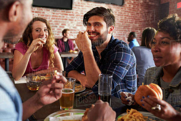 Friends eating out in sports bar with screens in background - Stock ...