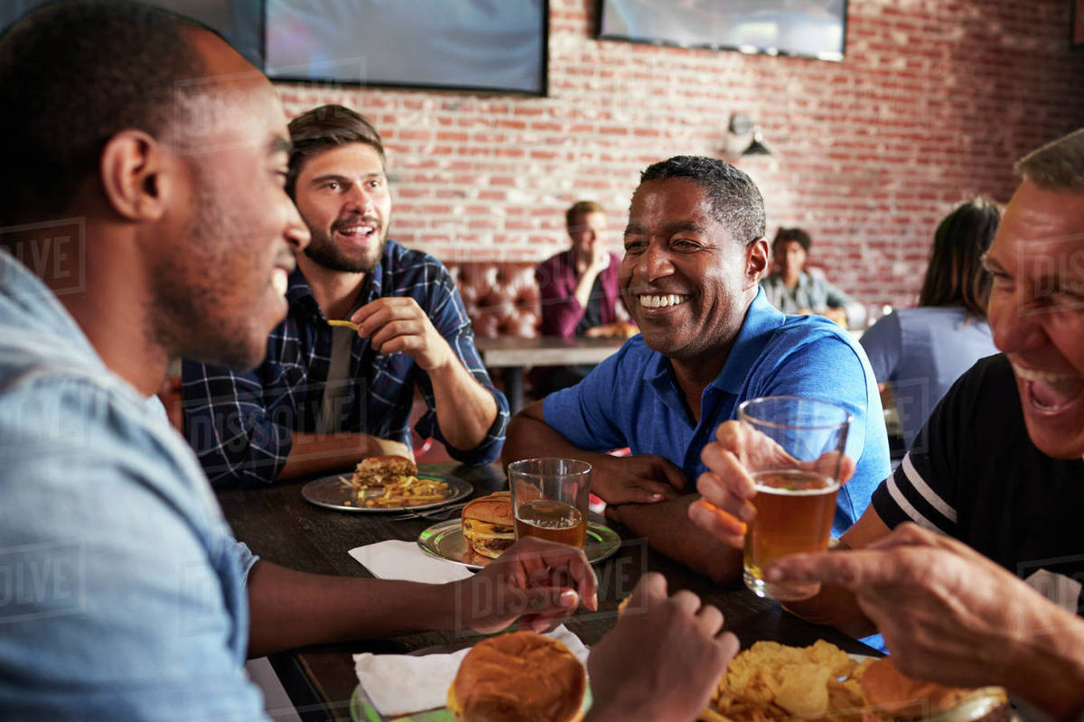 Male friends eating out in sports bar with screens in behind - Stock ...