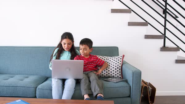 Brother And Sister Sitting On Sofa At Home Using Laptop Computer ...
