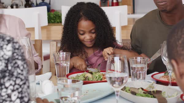 Multi-Generation Family Sitting Around Table At Home Enjoying Meal ...