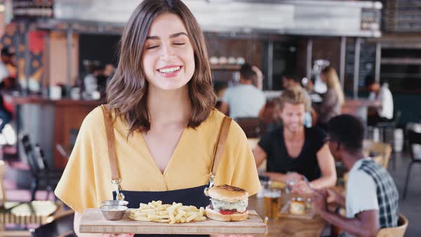 Portrait Of Waitress Serving Food In Busy Bar Restaurant Smiling At ...
