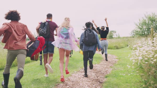 Group of young friends running through barriers at entrance to music ...
