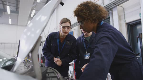 Female tutor with students checking oil level in car engine on auto ...