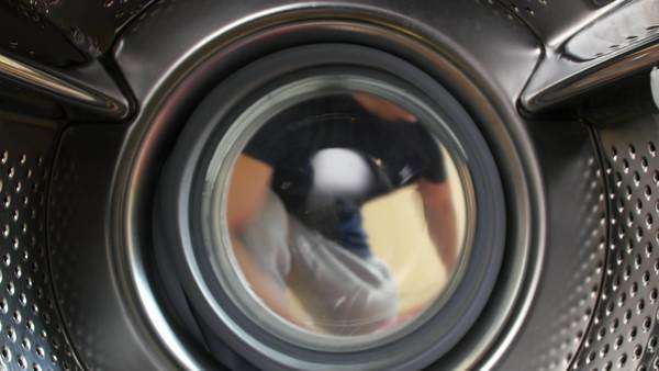 Man opens door of washing machine before loading laundry from basket ...