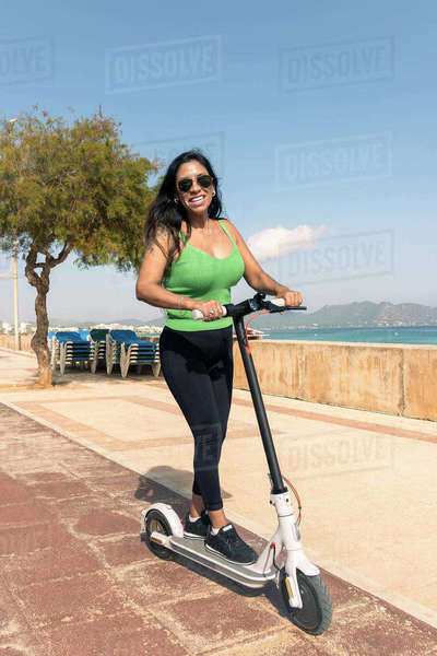 Woman riding electric scooter, happy and summer ride at tropical island ...