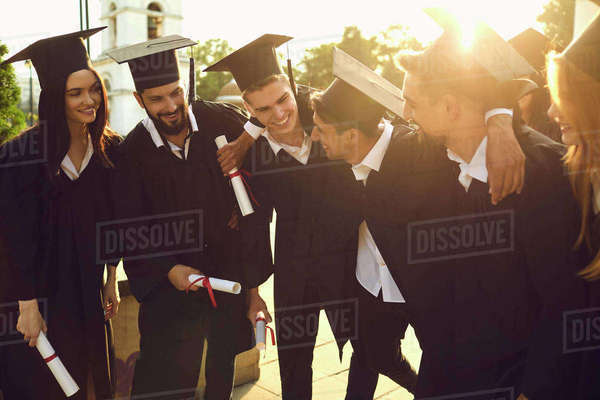 Happy and successful university graduates in academic gowns hold ...