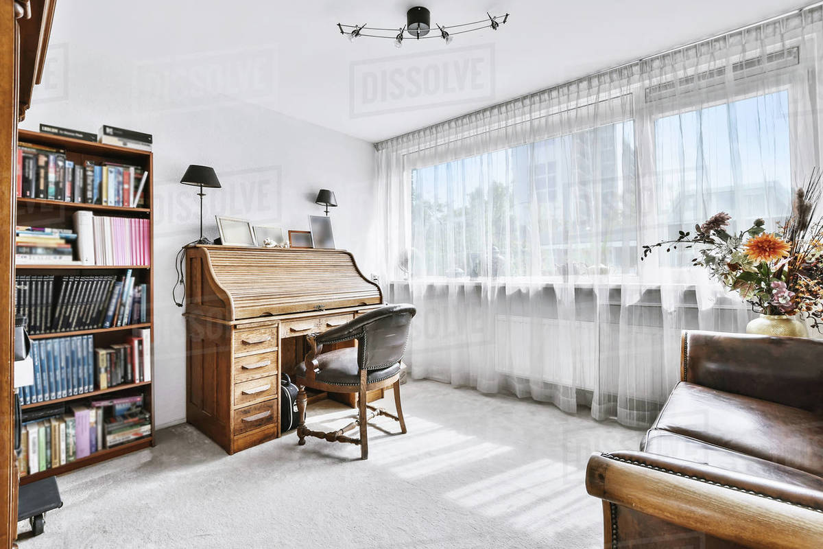 Sun lit white room with wooden secretary desk and armchair near ...