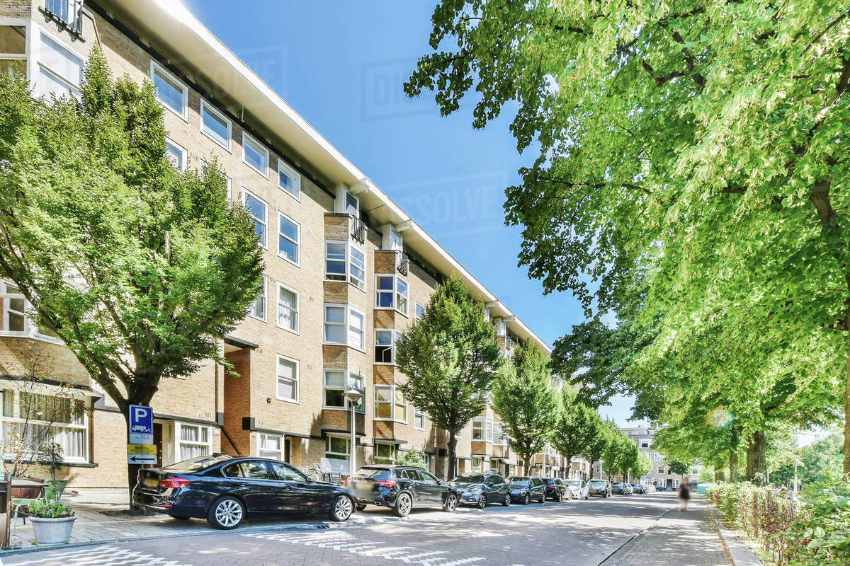 Modern brick apartment building located on city street with green trees ...