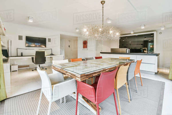 Stylish table with colorful chairs placed against workplace and kitchen ...
