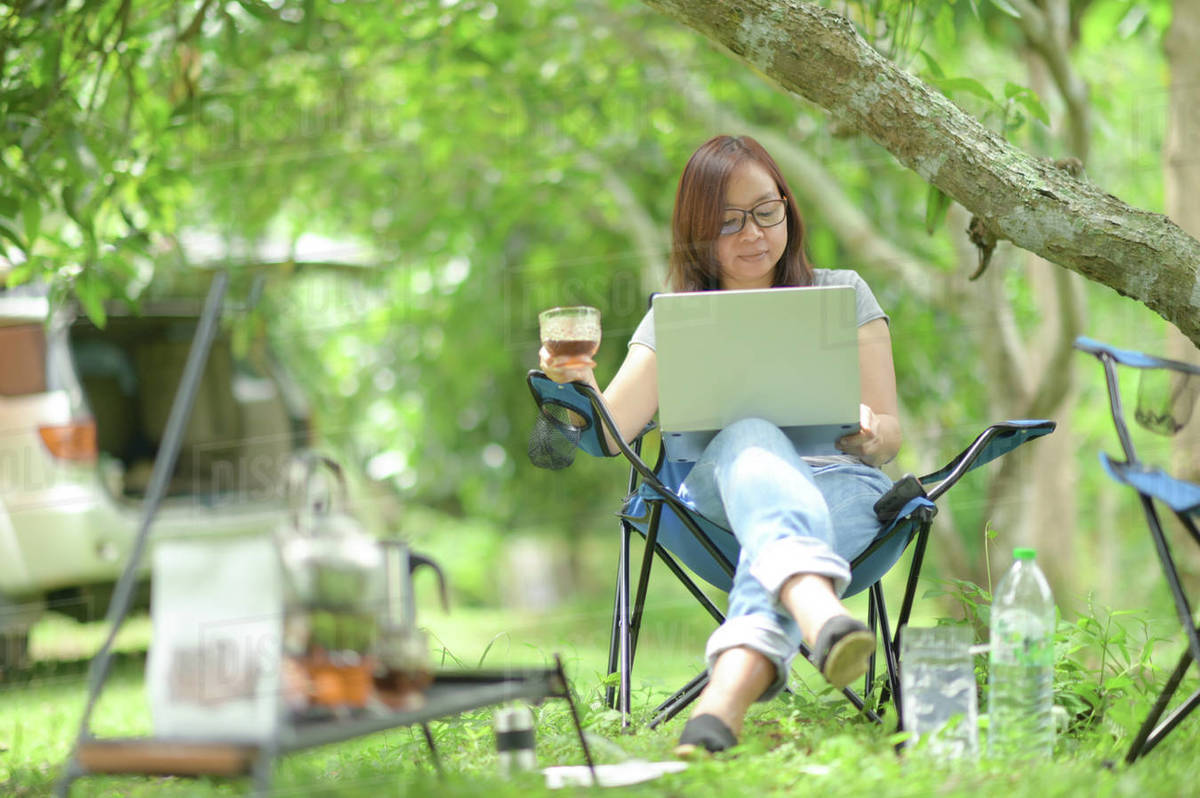 A woman working with a laptop during camping, wearing glasses and a ...