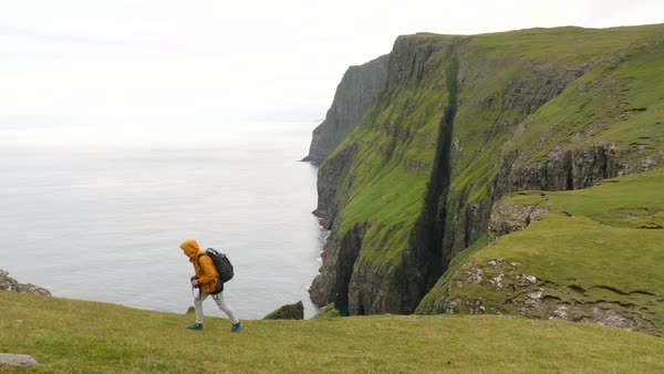Drone footage of a man walking on the edge of a cliff in Dunnesdrangar ...