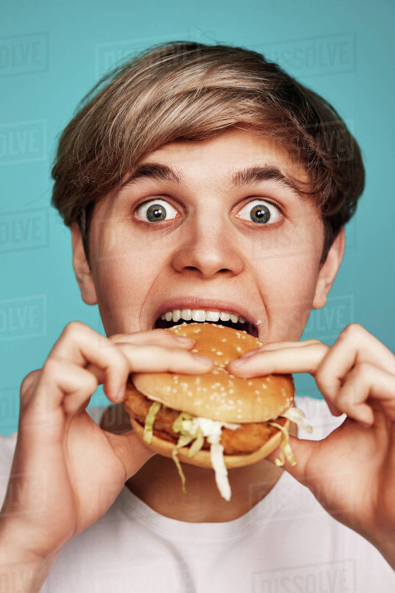 Very hungry young man eats tasty hamburger isolated on blue background ...