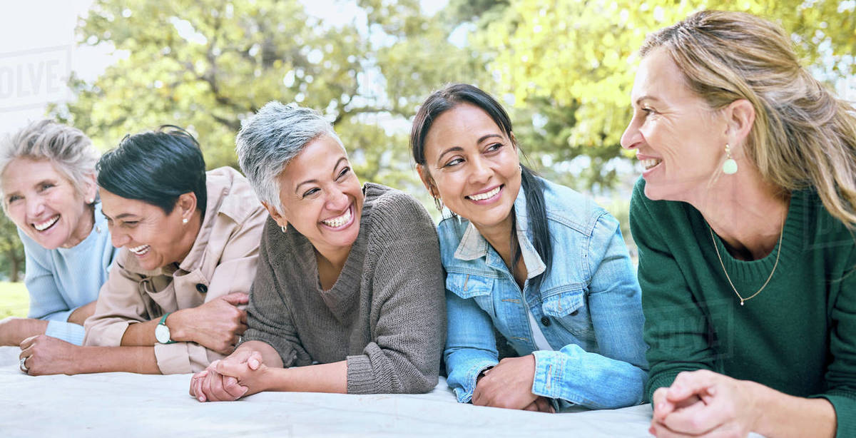 Happy, women and relax at a park, laughing and bonding while lying on a ...